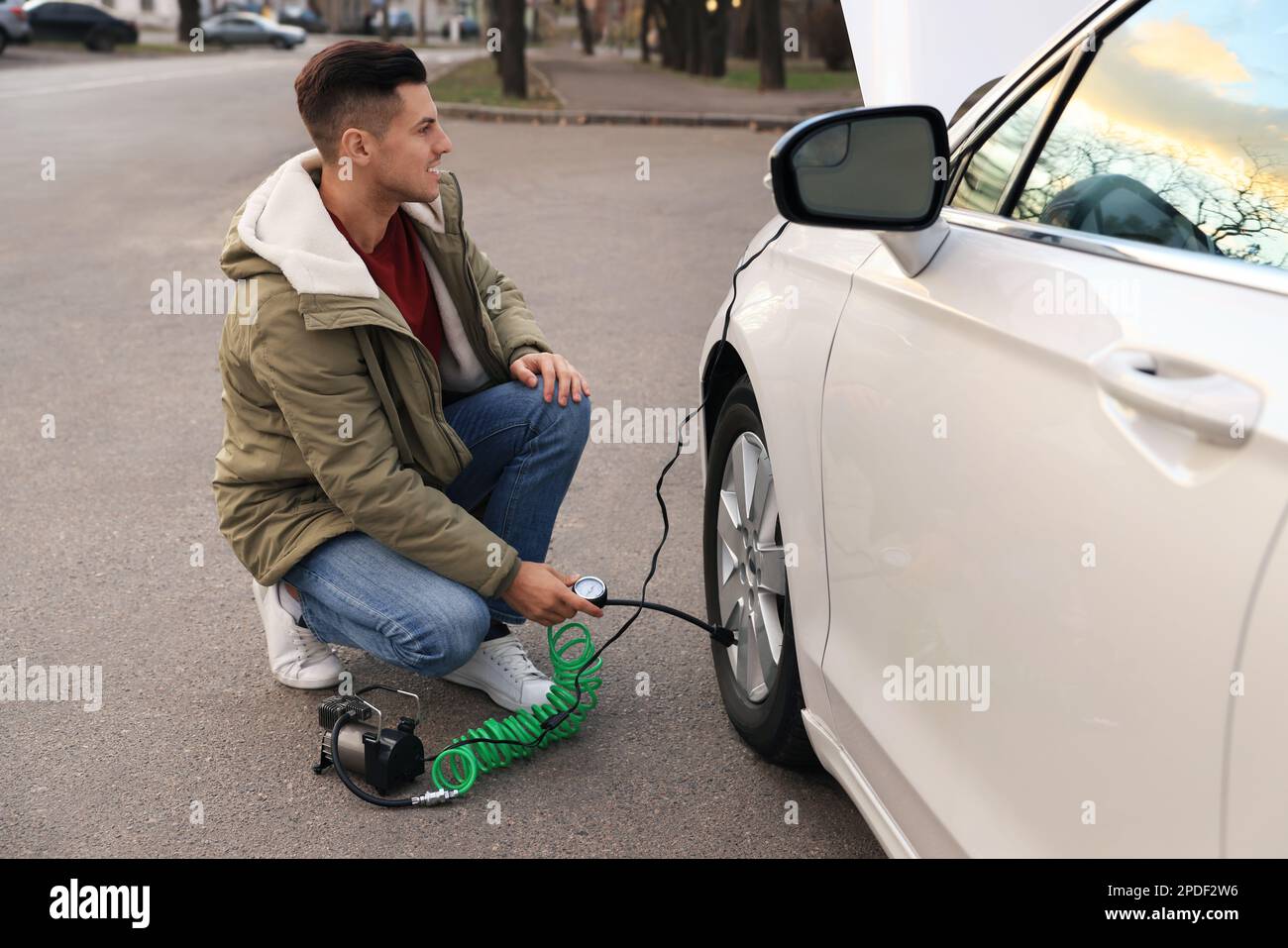 Handsome man inflating car tire with air compressor on street Stock ...