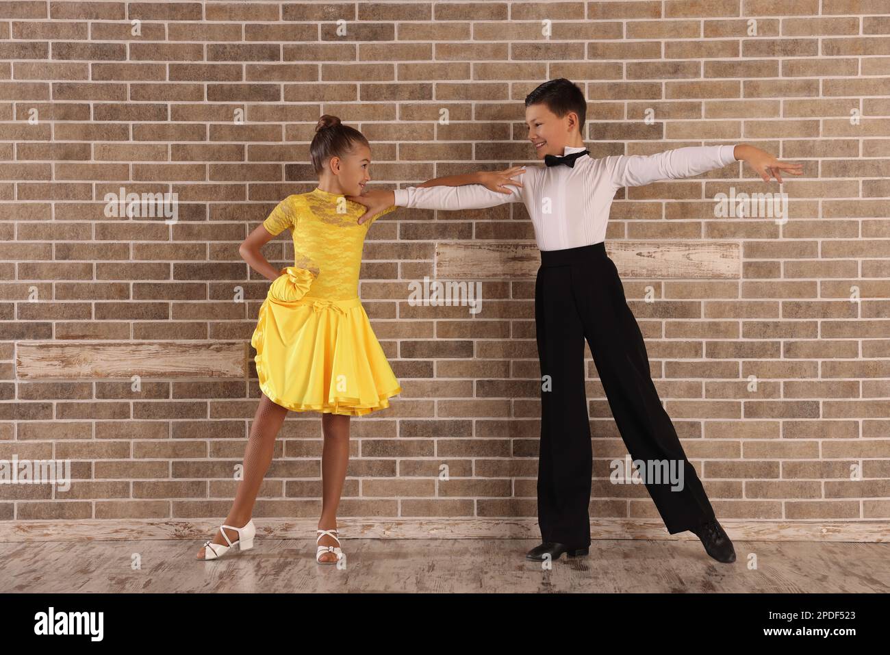 Beautifully dressed couple of kids dancing together near brick wall ...