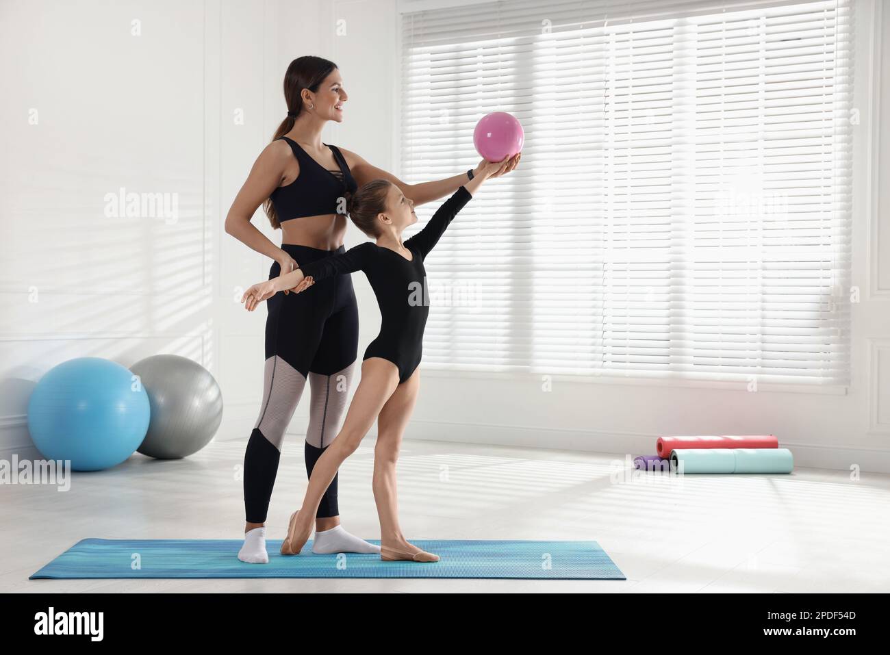 Gymnastic coach helping little girl to do exercise with ball indoors ...
