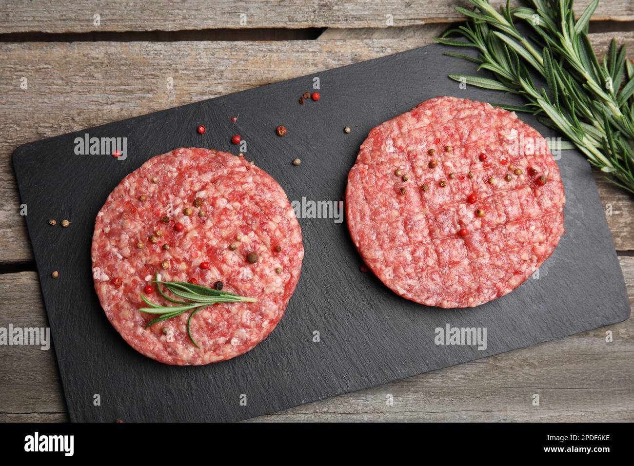 Raw hamburger patties with rosemary and peppercorns on wooden table ...