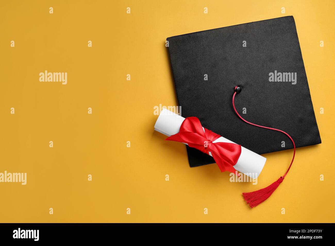 Graduation hat and diploma on yellow background, flat lay. Space for ...