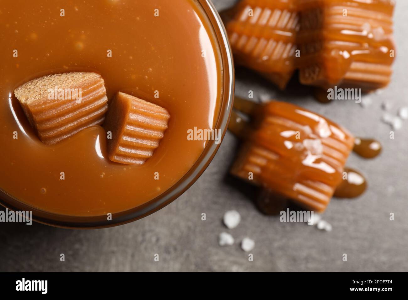 Tasty salted caramel with candies in glass bowl on grey table, top view ...