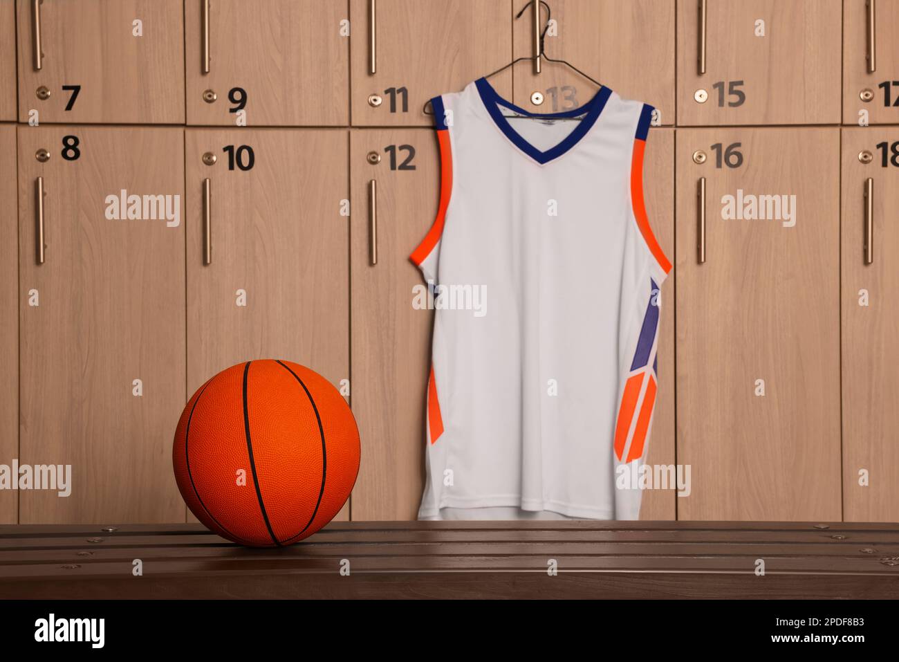 Orange basketball ball on wooden bench and hanger with uniform in ...