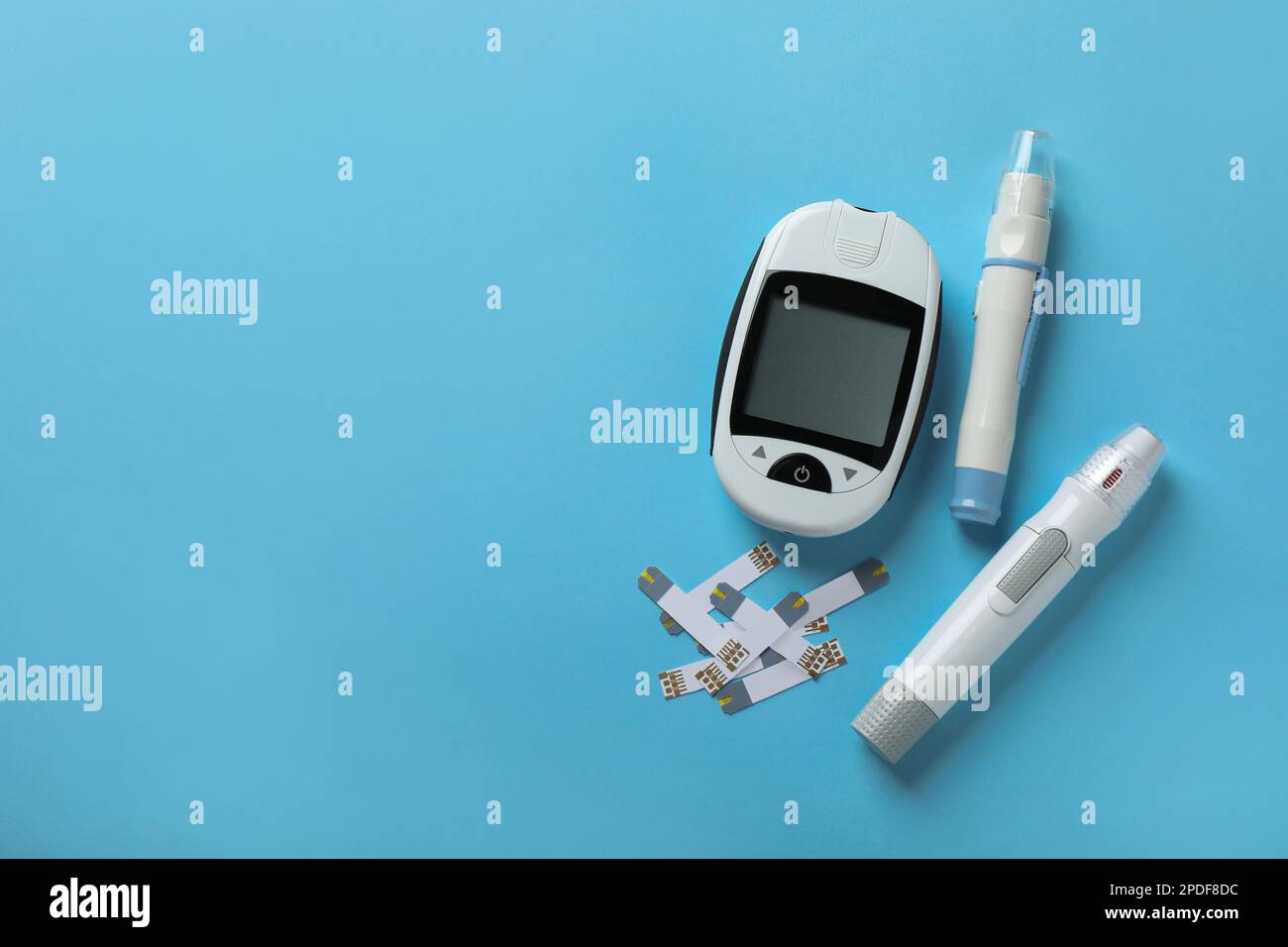 Digital glucometer, lancet pens and test strips on light blue ...