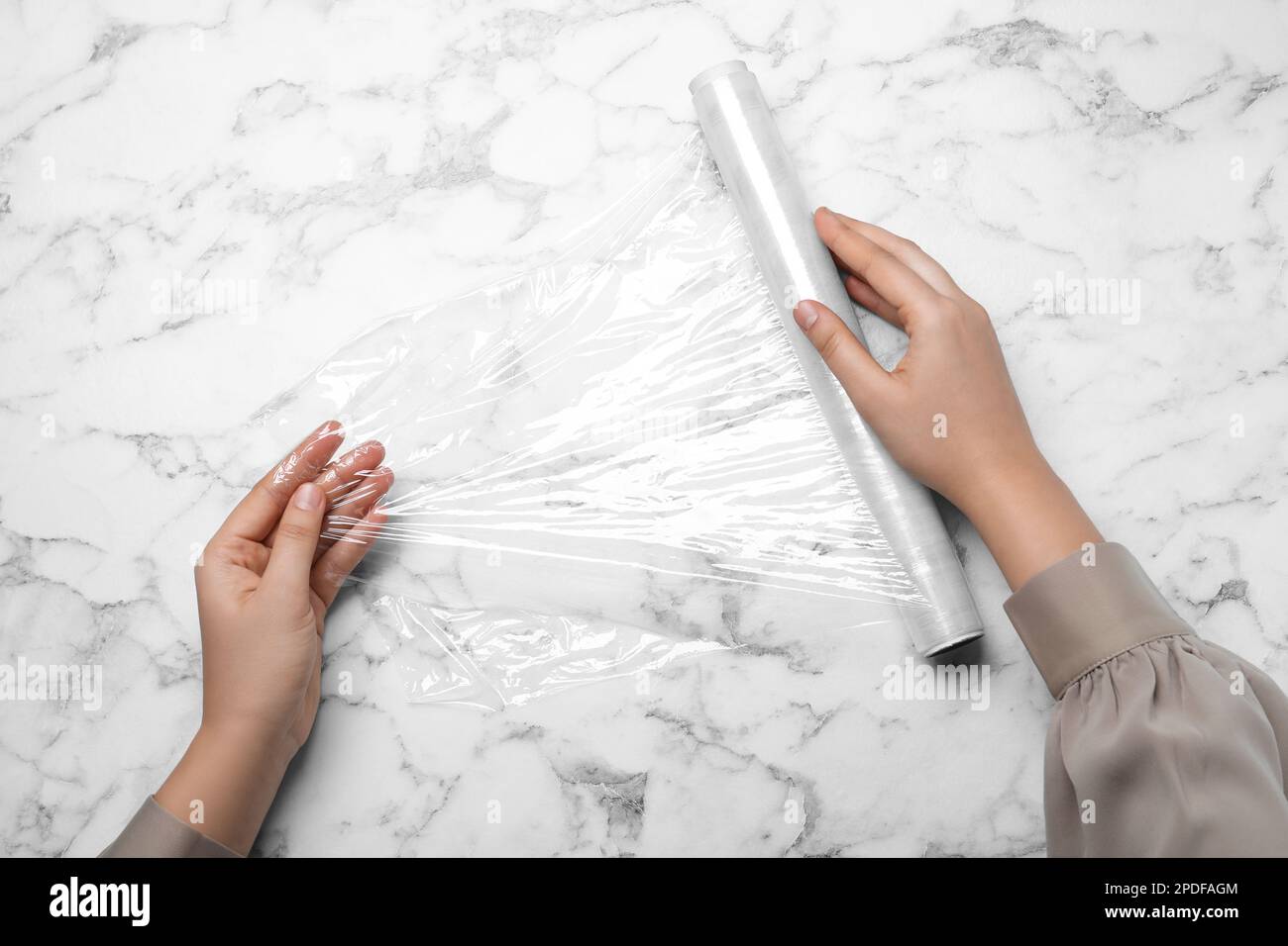 Woman with roll of stretch wrap at white marble table, top view Stock ...