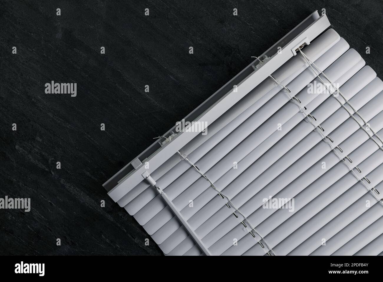 Stylish horizontal window blinds on black table, top view. Space for ...
