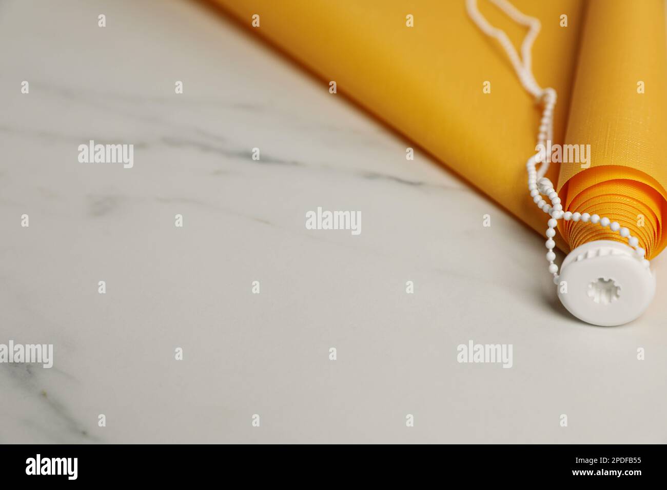 Stylish roller window blinds on white marble table, closeup. Space for ...