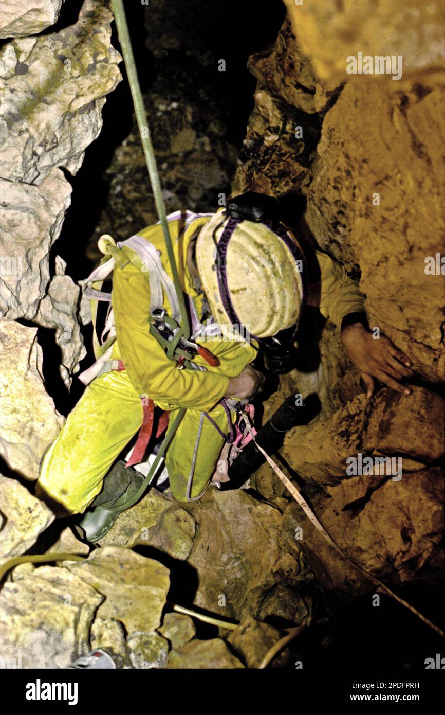 A speleology enthusiast is descending with a rope inside a cave near ...