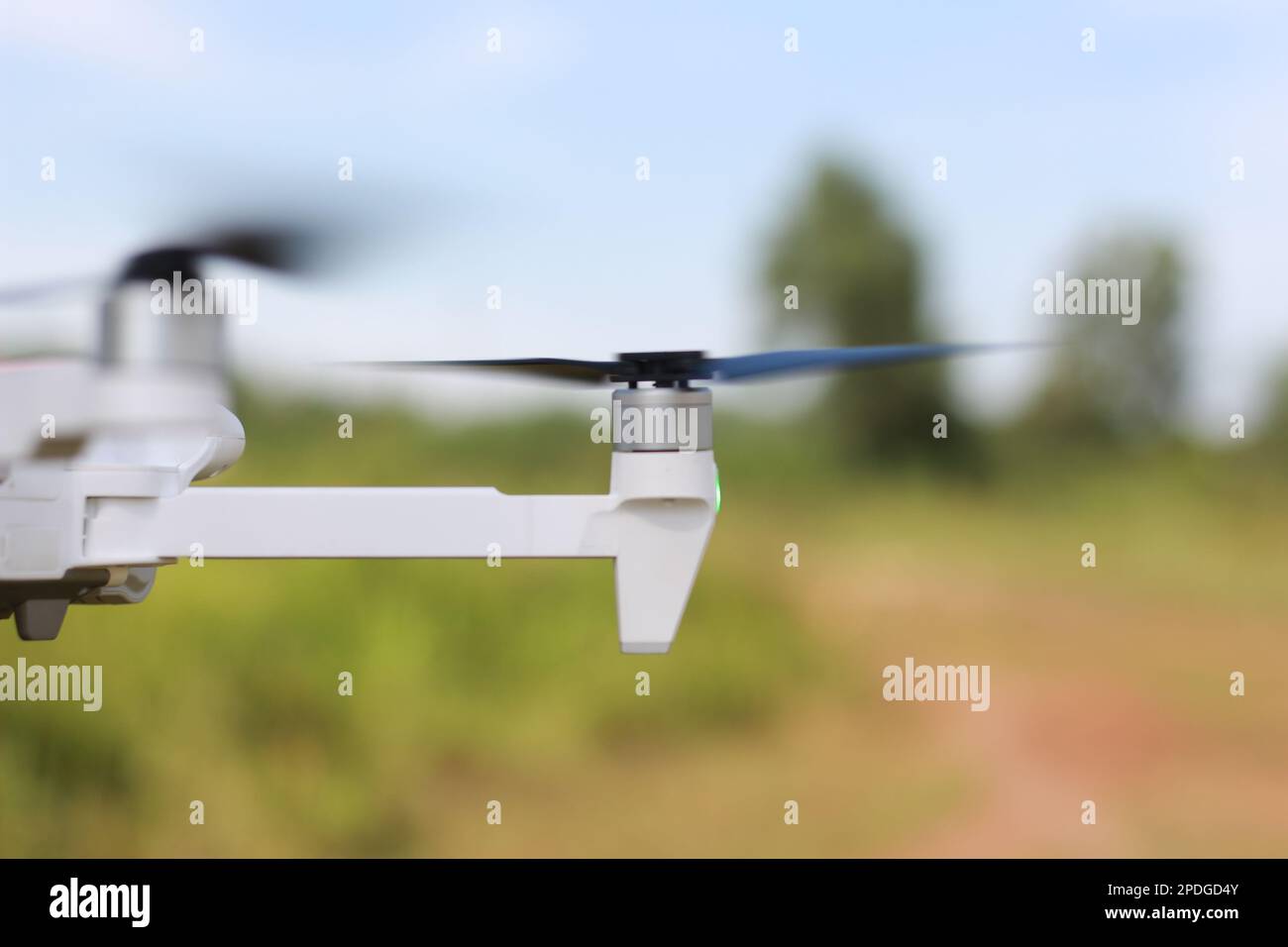 a photo of a drone flying with a blurry propeller against a green open ...