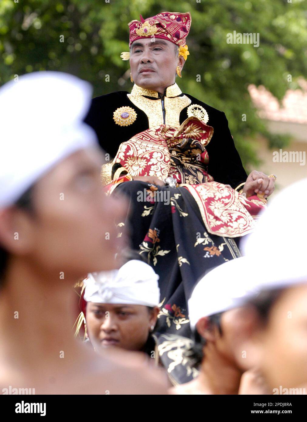 The king of Denpasar Ratu Ida Tjokorda IX sits as Balinese man carrying ...
