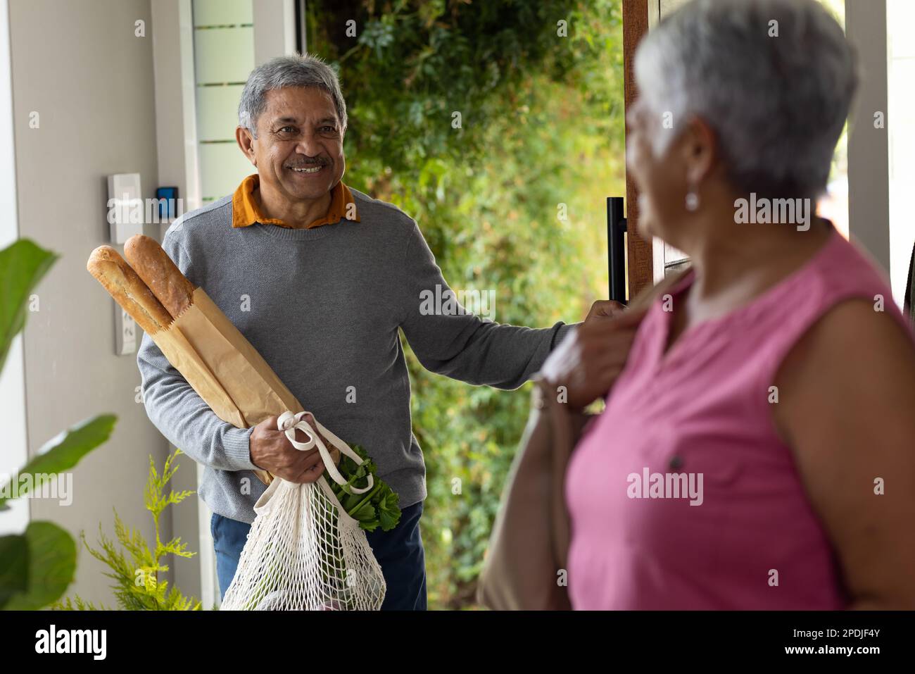 Smiling biracial senior man carrying bread and groceries in mesh bag ...