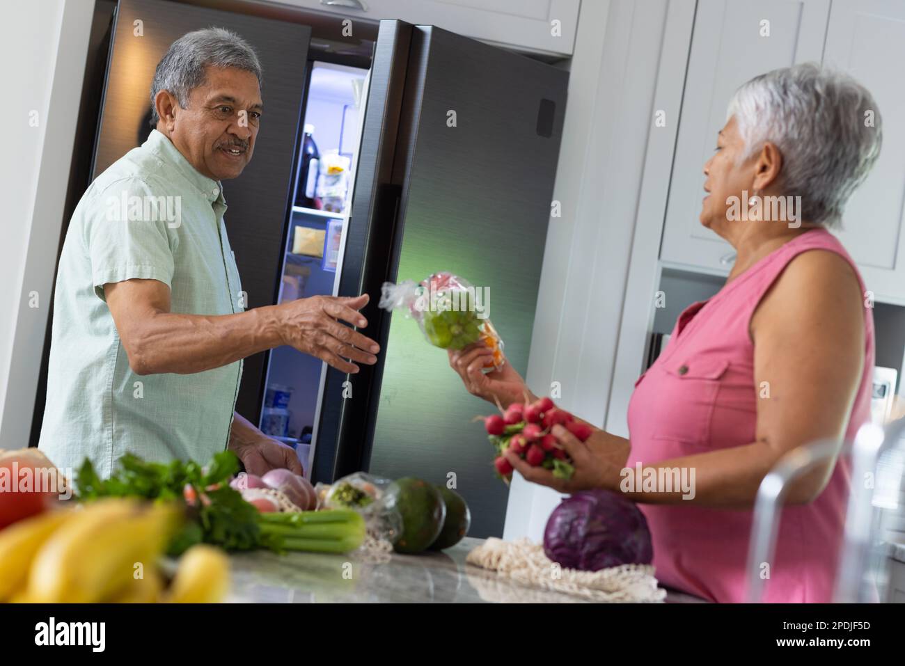 Biracial senior woman giving fresh vegetables to husband for keeping in ...
