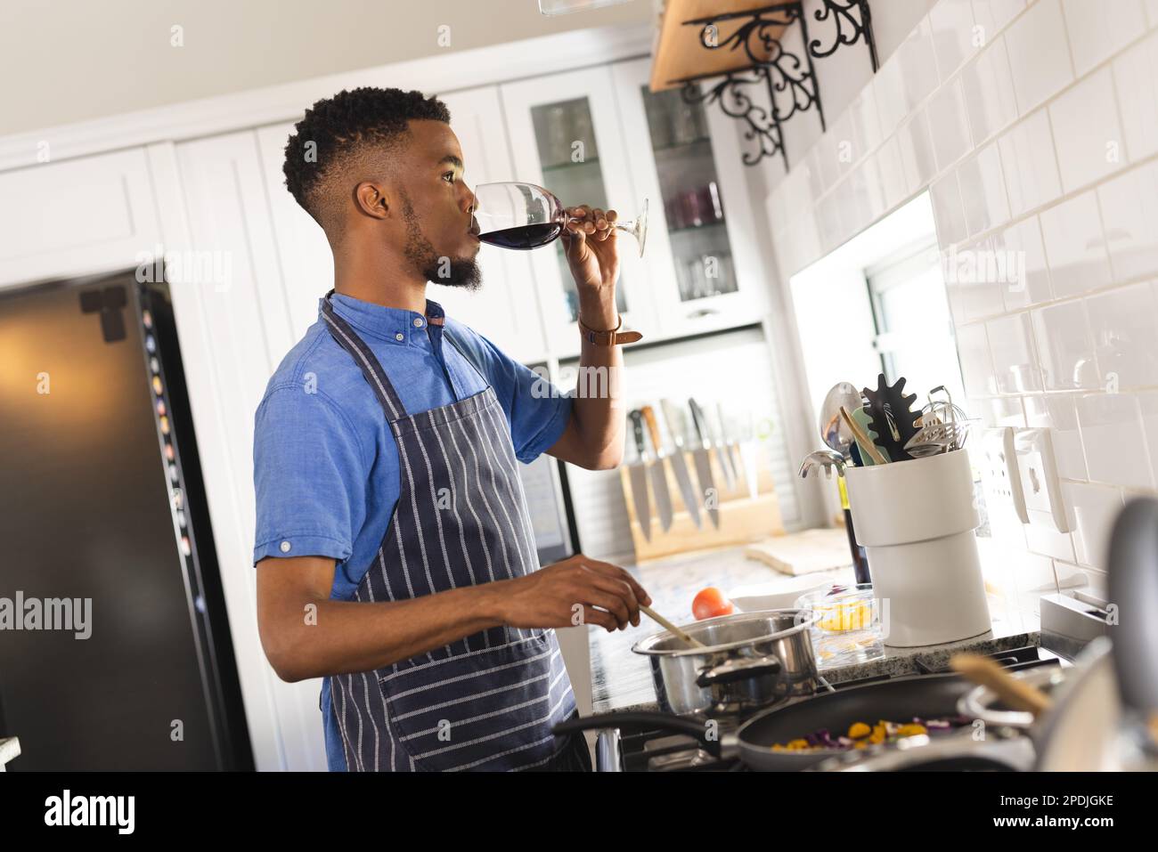 Happy african american man cooking dinner and drinking red wine in ...