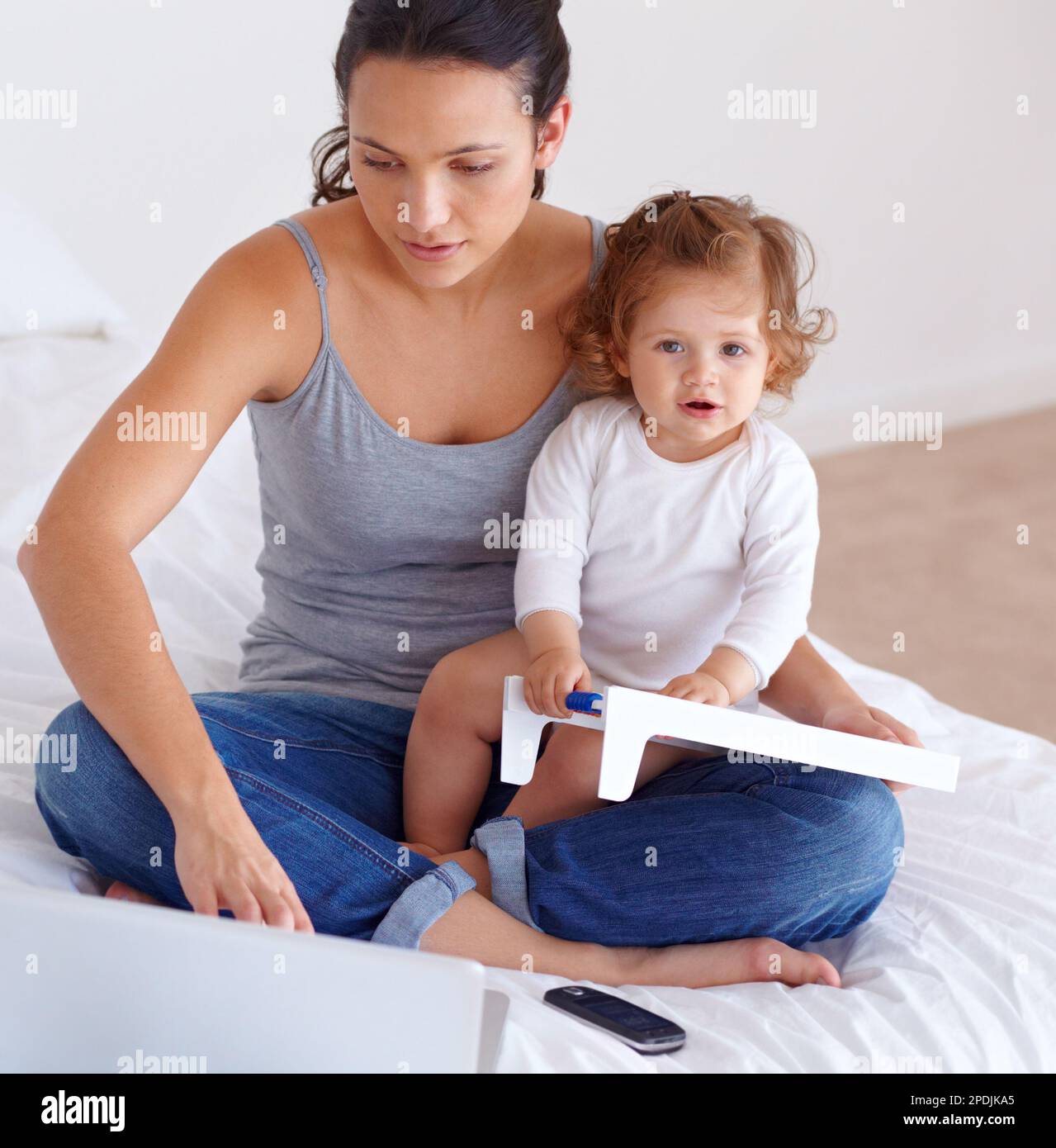 Learning at home. A young mother working on her laptop while her baby ...