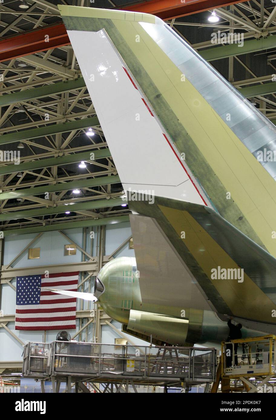 The massive tail fin of a 747 airplane dwarfs a worker at lower right ...
