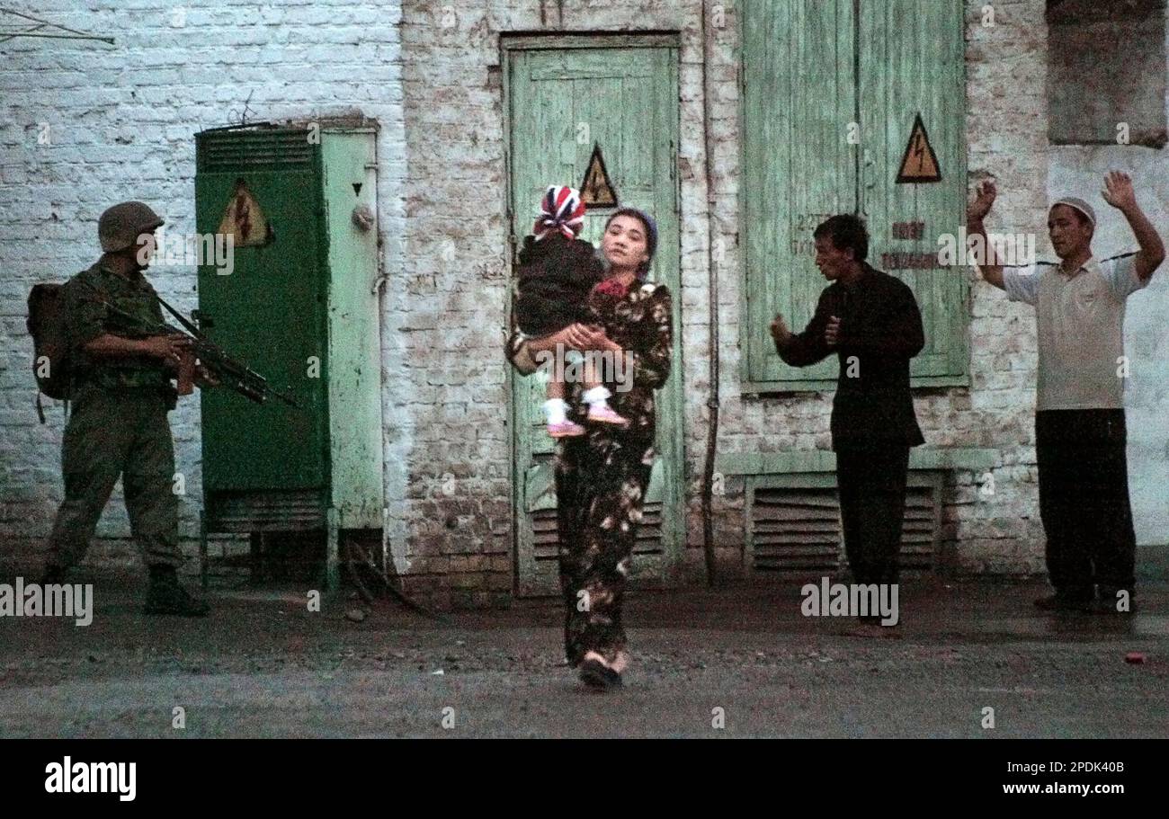 ** FILE ** A local resident carrying a child, walks by a Uzbek soldier ...