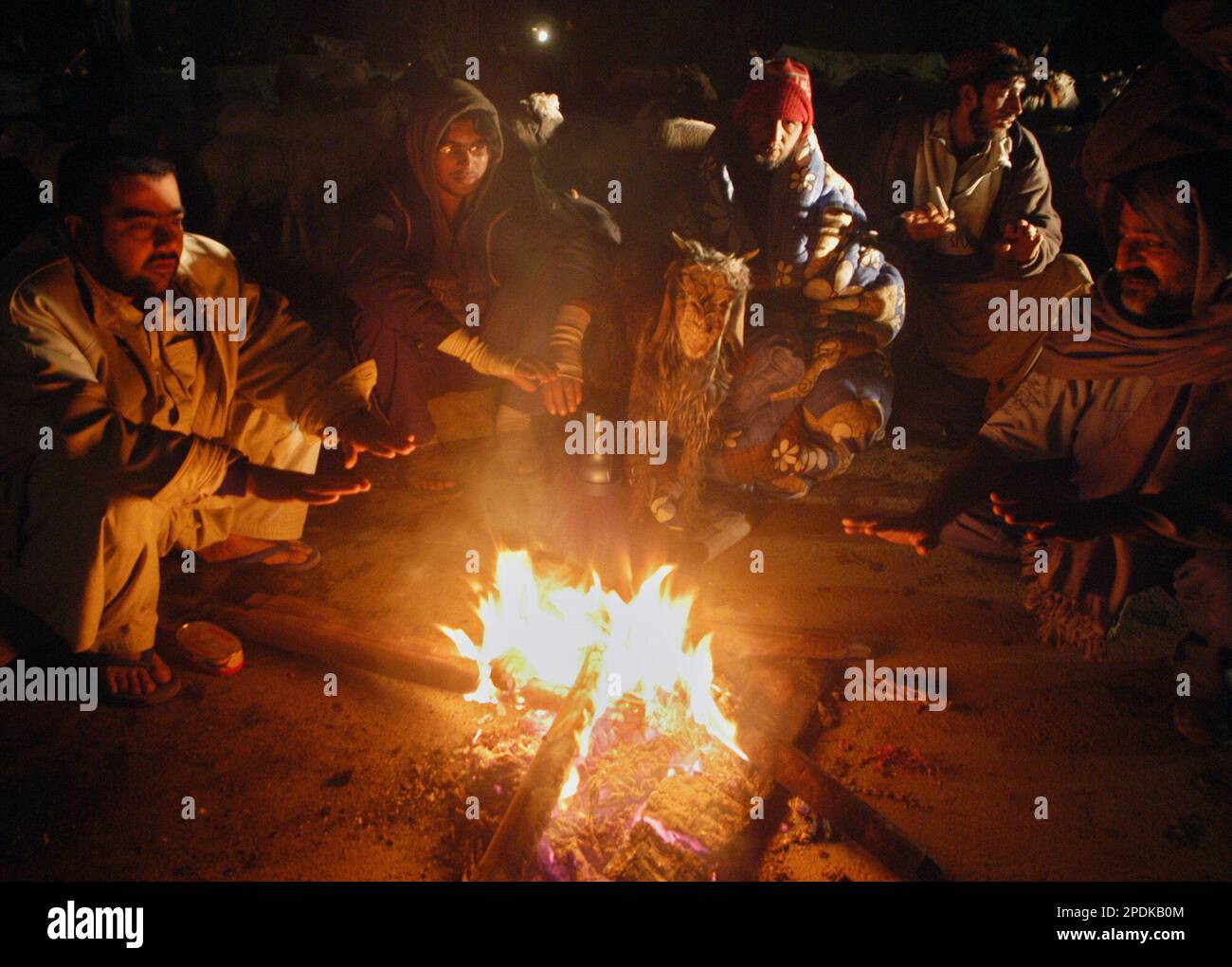 Pakistani earthquake survivors sit around the fire for warmth at a camp ...