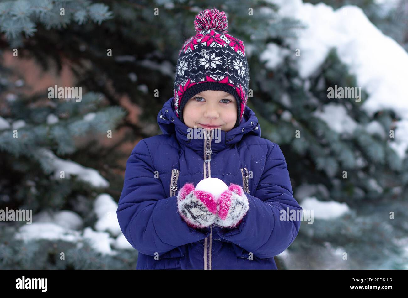 Smiling child holding snowball in hands looking at camera in winter ...