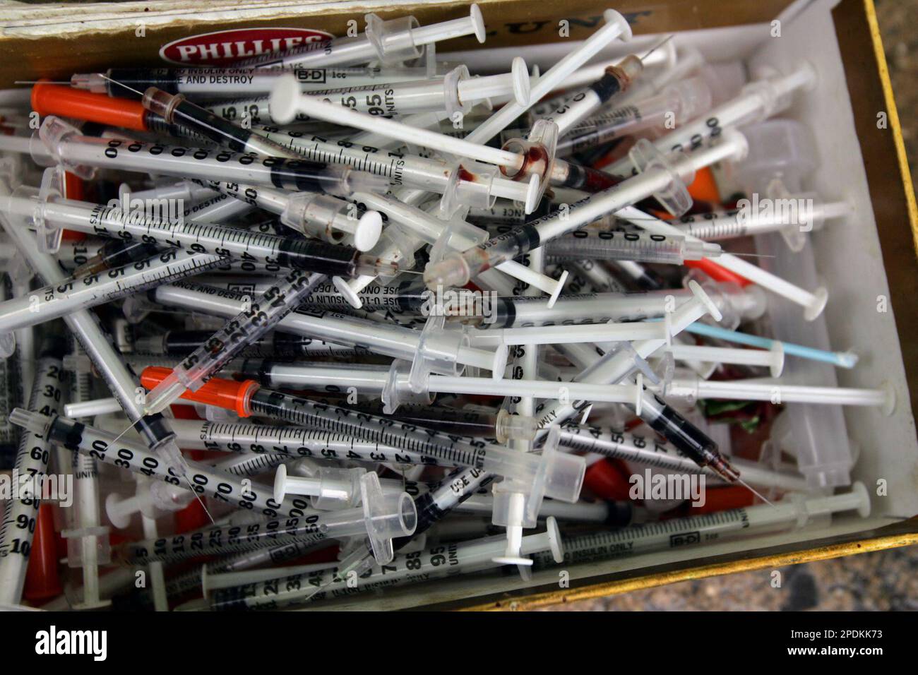 Used syringes fill a cigar box carried by an addict preparing to ...