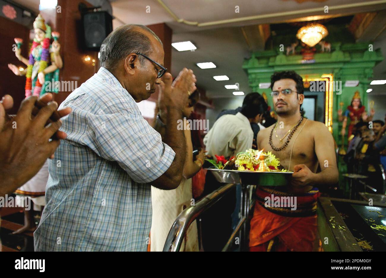 Hindu devotees offers prayer while a priest gives out coconut and ...