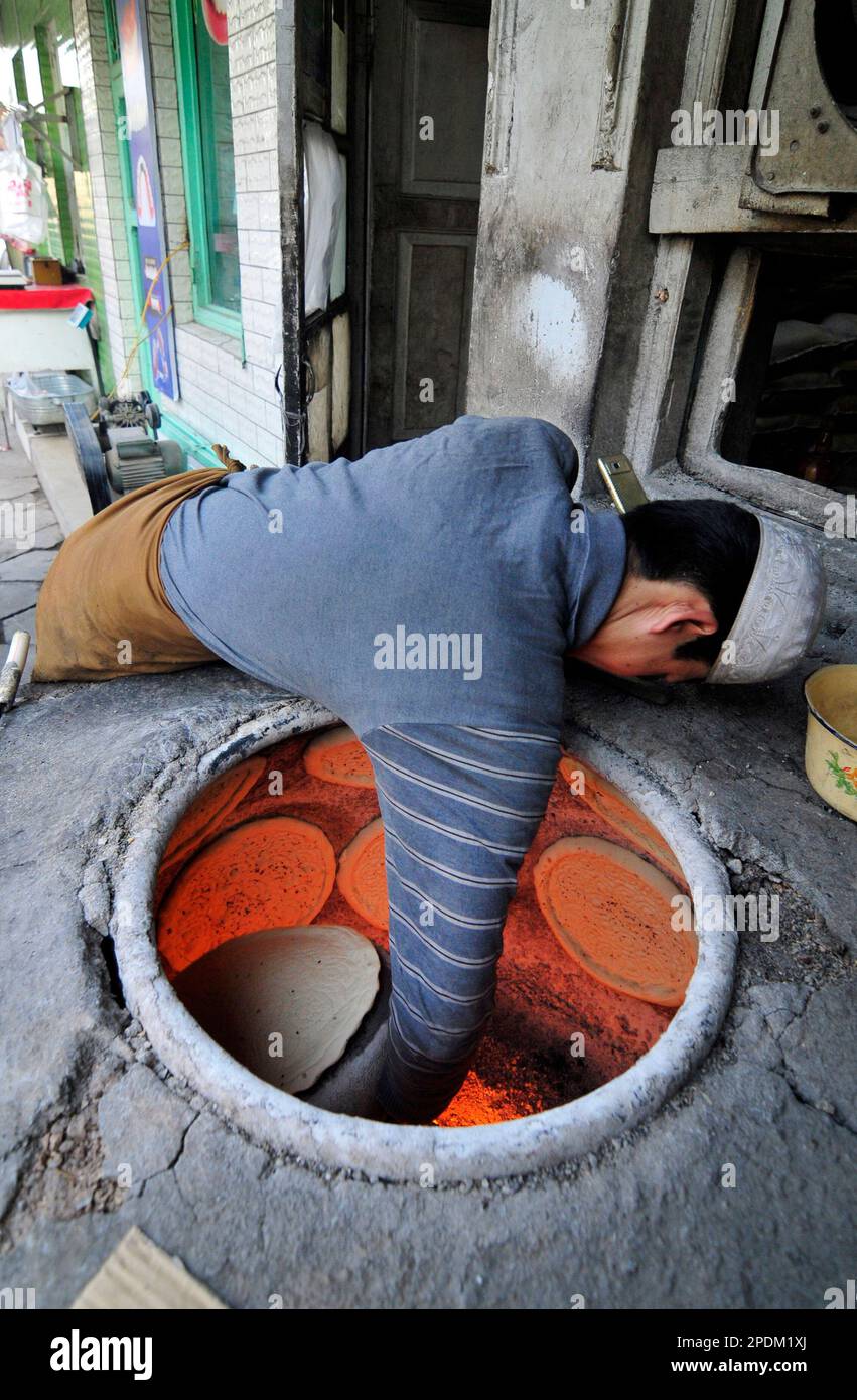 An Uyghur man baking the Naan bread in a tandoor oven in the old city ...