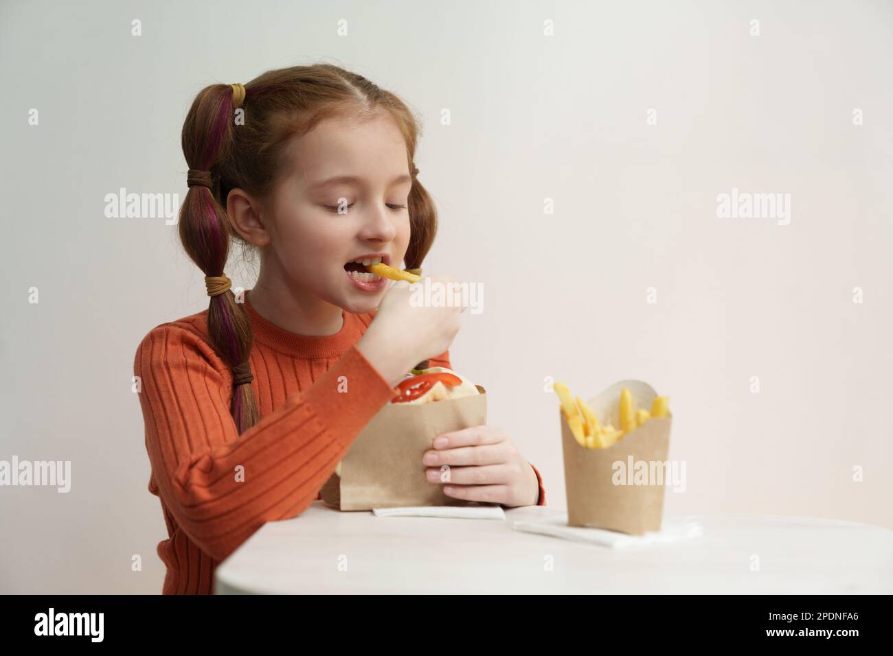 Adorable little girl eating fries and sandwich in a cafe. Portrait of ...