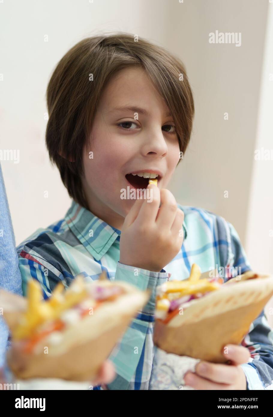 Happy white boy eats fast food for lunch. Portrait of cute elementary ...