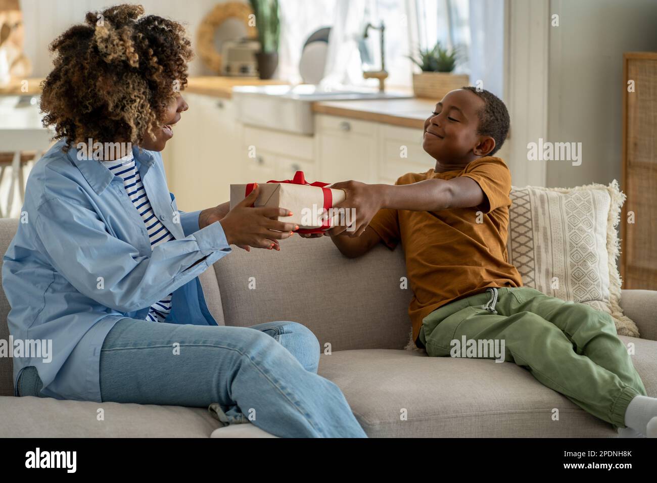 Happy African American child son surprising mom on Mothers Day at home ...