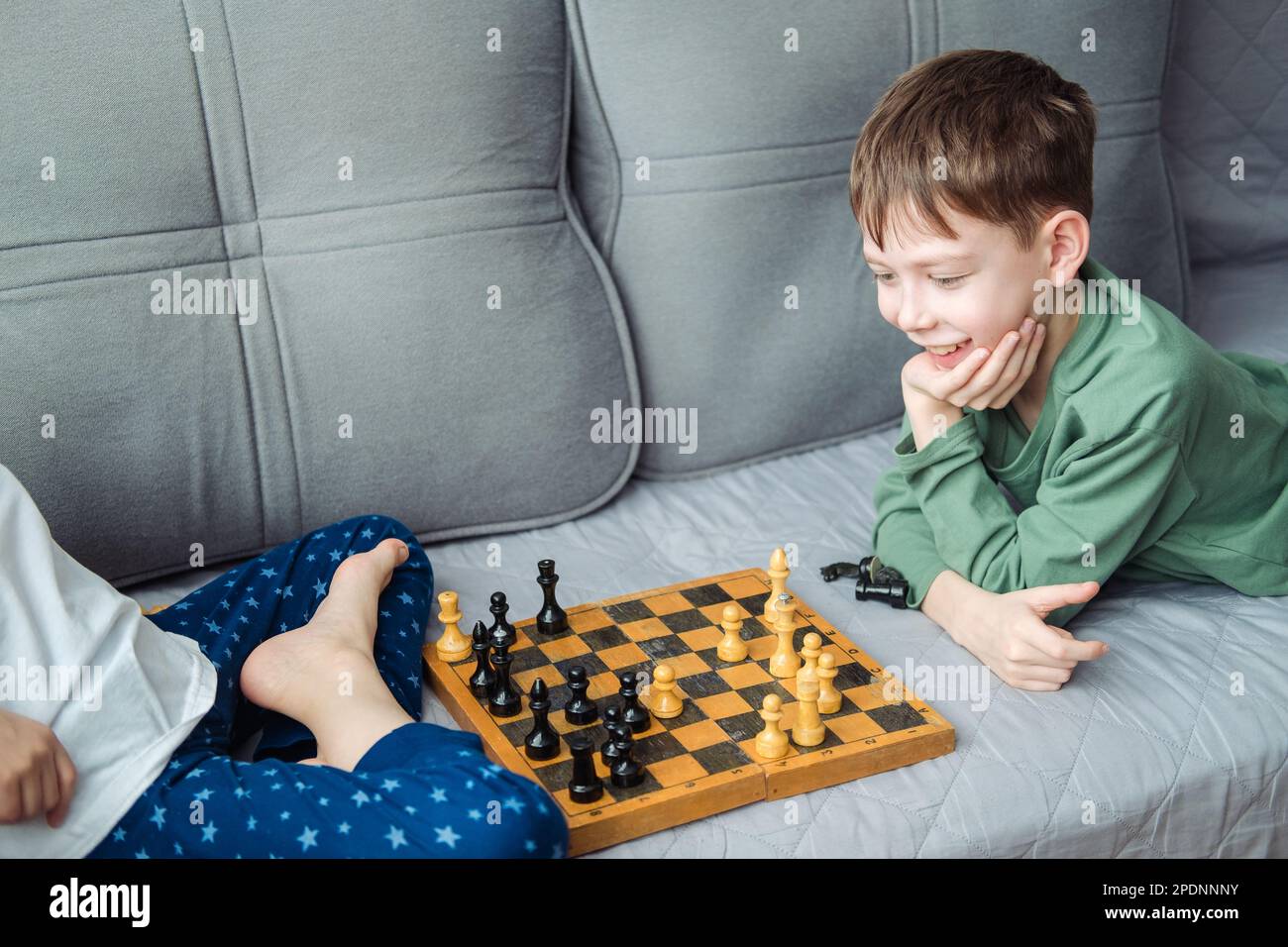 Boys play wooden chess lying on a gray sofa Stock Photo - Alamy