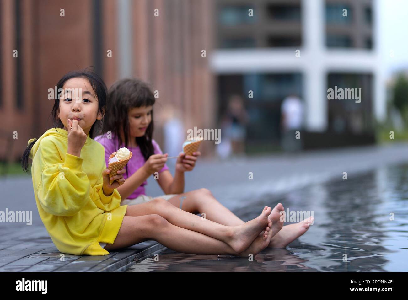 Two girls sitting, having legs in fountain, enjoying ice cream and ...