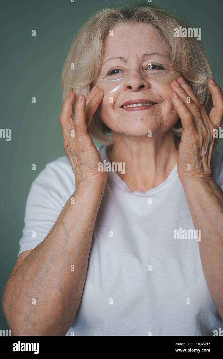 Smiling old caucasian woman with natural beauty applying patches under ...
