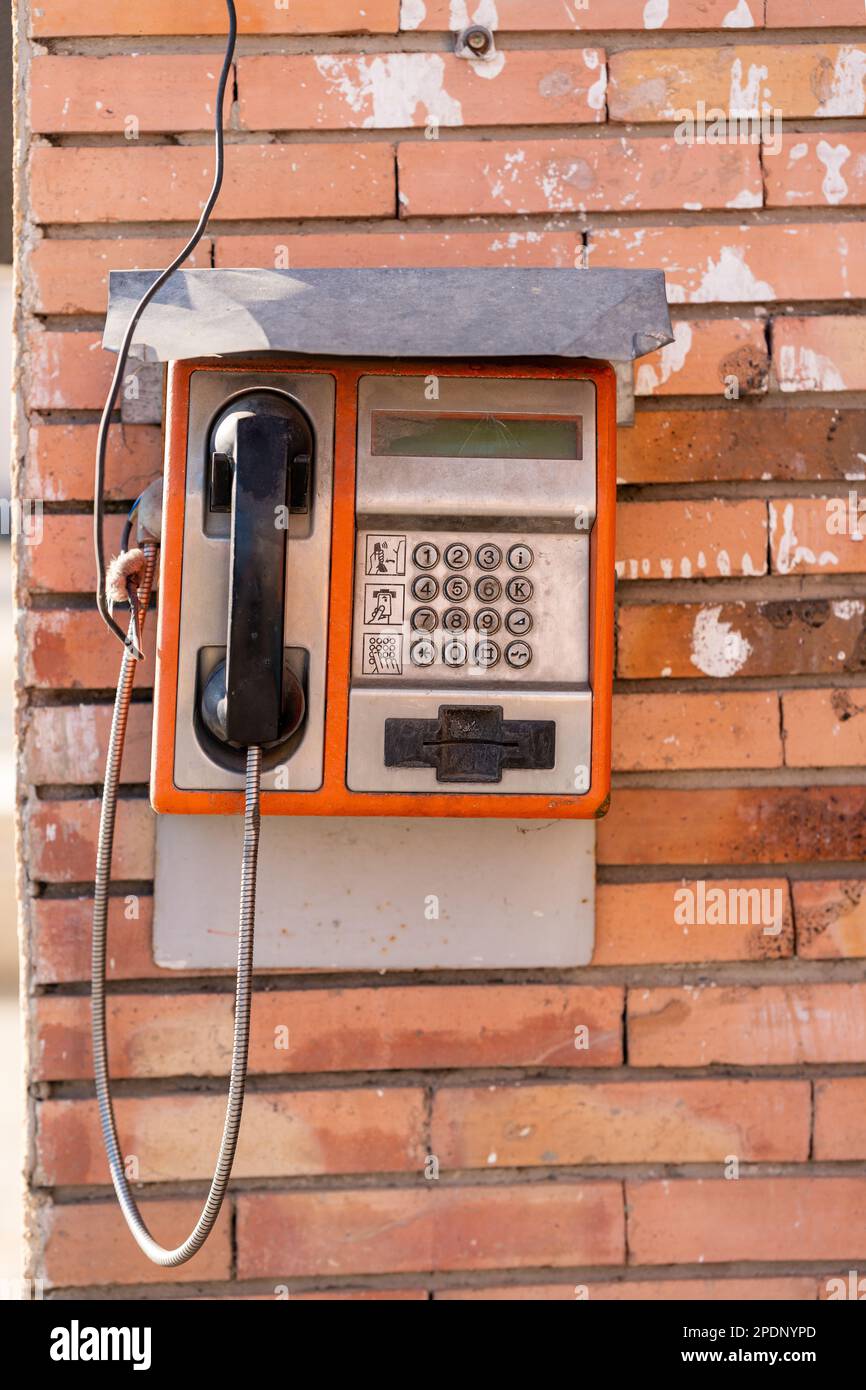 An old payphone stands against a brick wall in an empty parking lot ...