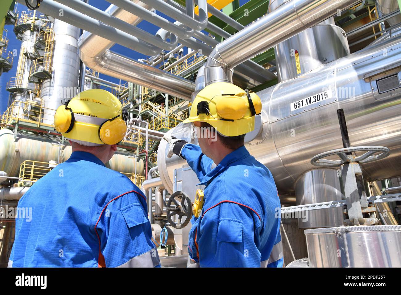 group of industrial workers in a refinery - oil processing equipment ...