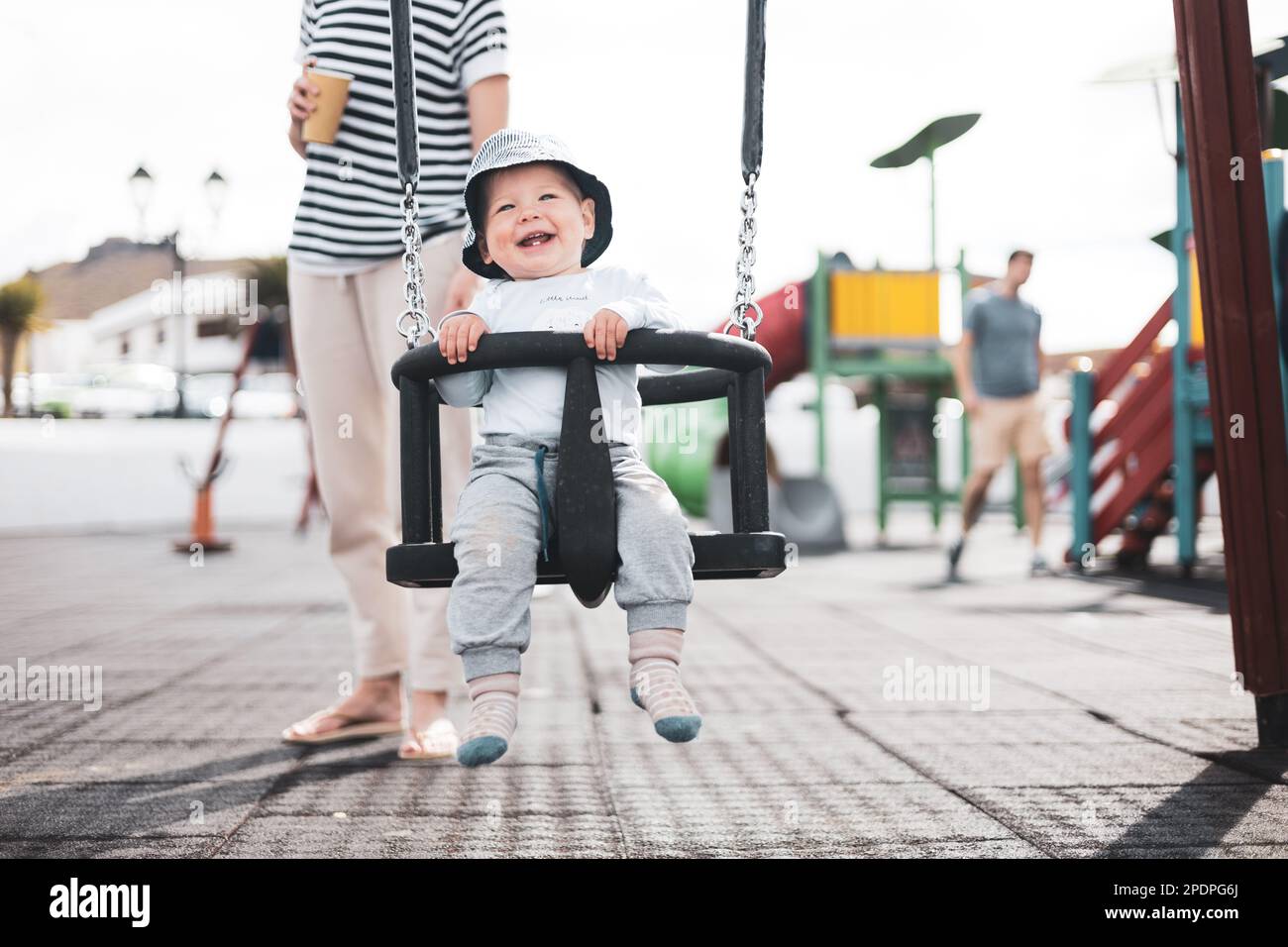 Mother pushing her infant baby boy child on a swing on playground ...