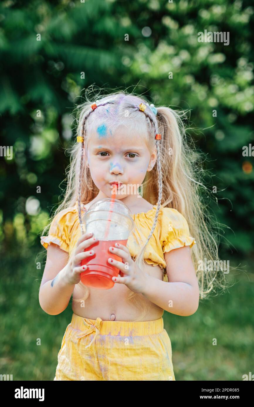 Outdoor portrait of Funny grimy little girl with two ponytails drinks ...