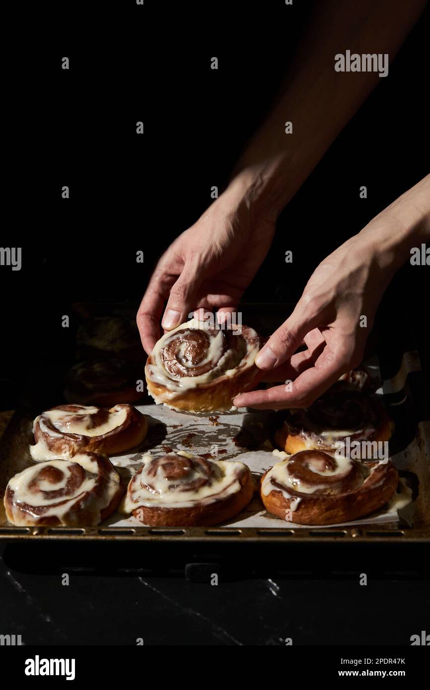 Cinnabon rolls on black background. Hand touches cinnabon from the top ...