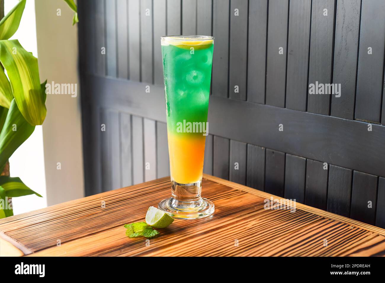 Rainbow yellow green alcohol cocktail on wooden table against dark wall ...