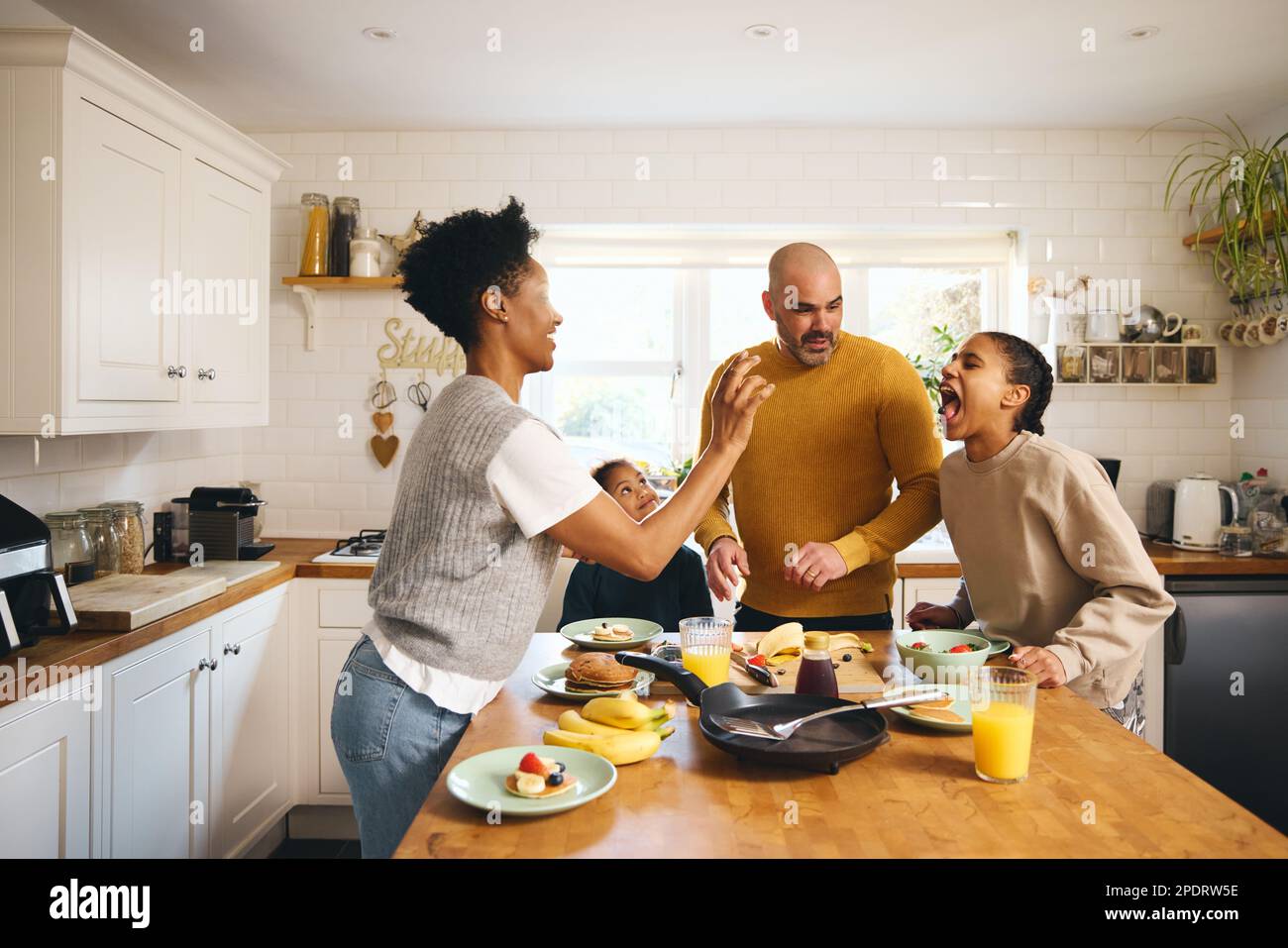 Mother aiming to throw food towards daughter's open mouth at family ...