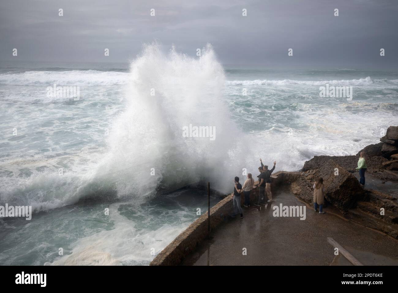 Onlookers watching Atlantic Ocean wave breaking over seafront wall ...