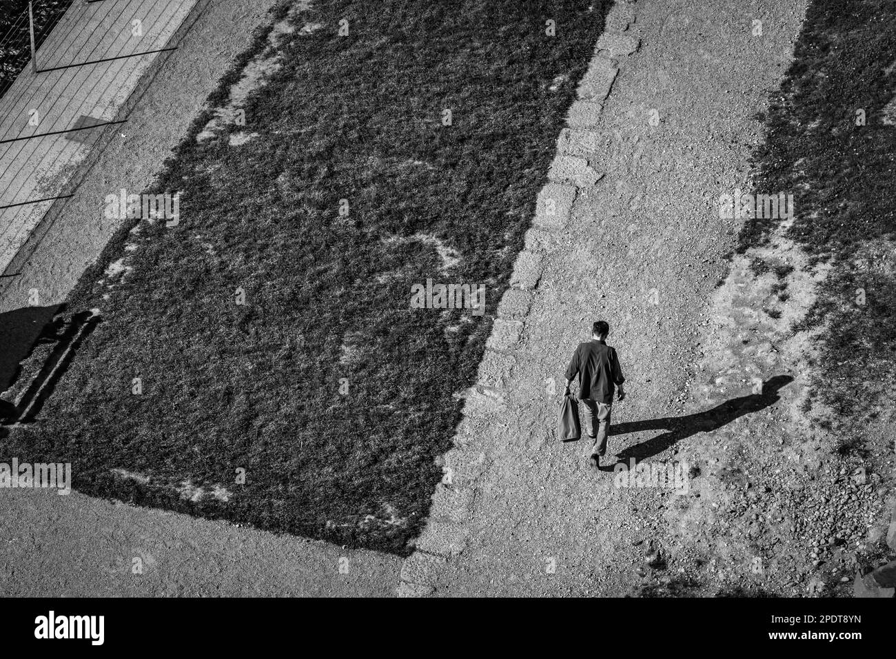 Old man walking on an alley next to the street with his shadow to the ...