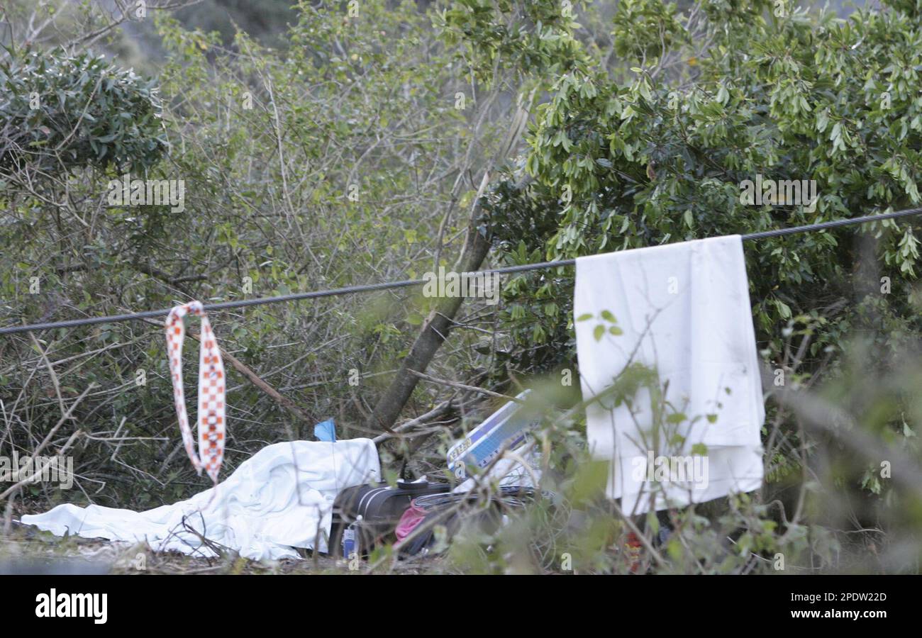 A body covered by a white tarpaulin lies on the ground at the scene of ...