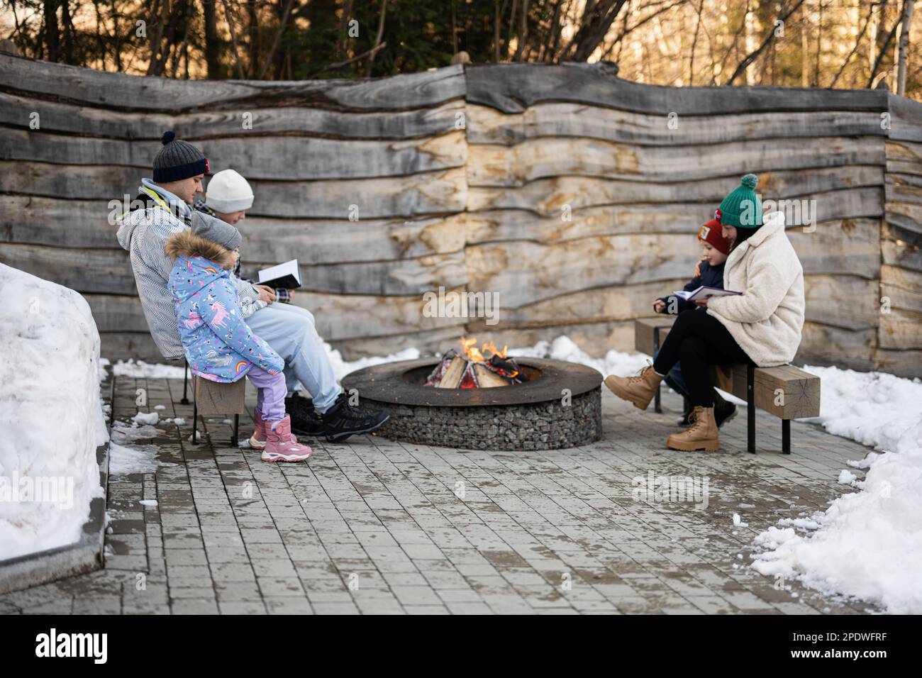 Family with three kids sitting by camp bonfire and read books on winter ...