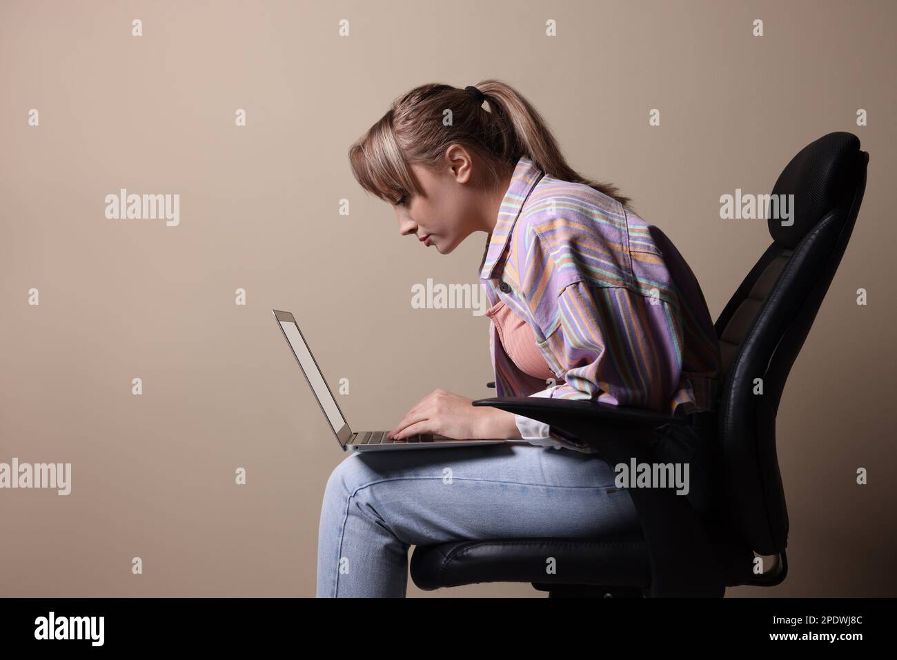 Young woman with poor posture using laptop while sitting on chair ...
