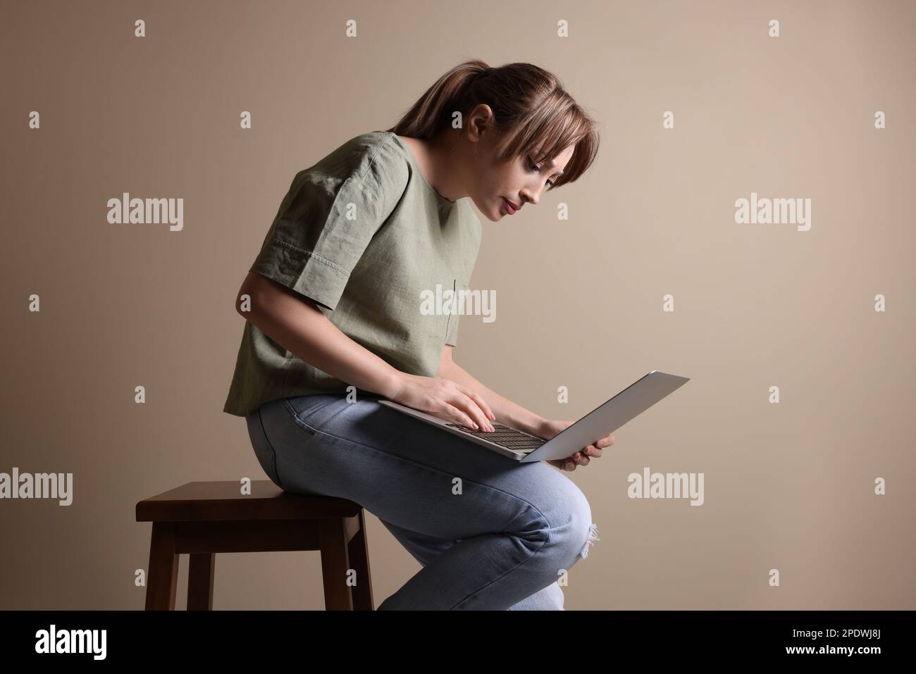 Young woman with poor posture using laptop while sitting on stool ...