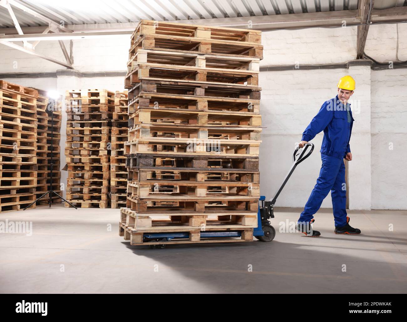 Worker moving wooden pallets with manual forklift in warehouse Stock ...