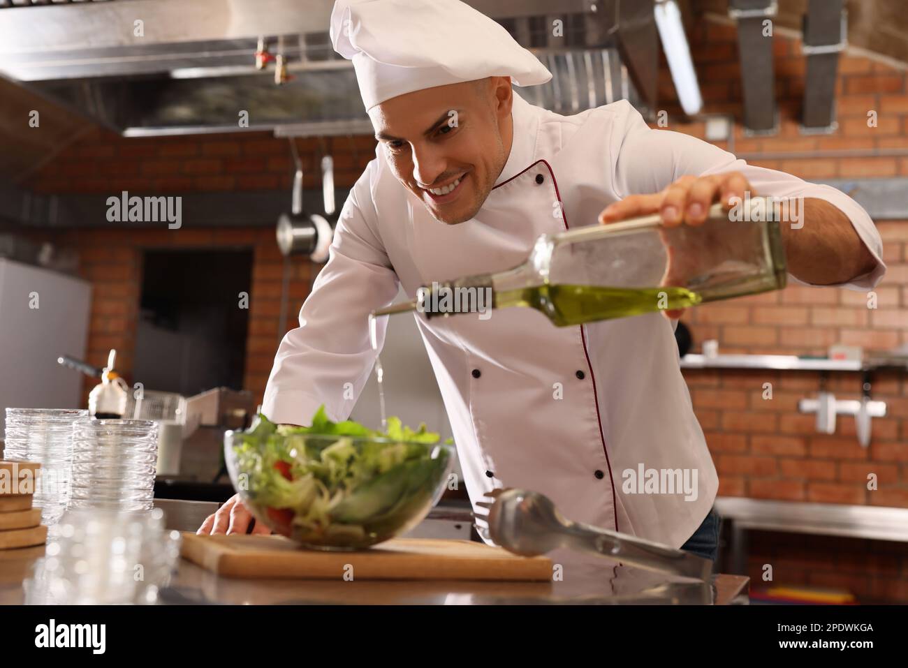 Professional chef pouring oil into bowl with fresh salad in restaurant ...