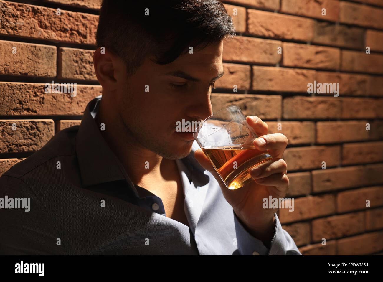 Addicted man drinking alcohol near red brick wall Stock Photo - Alamy