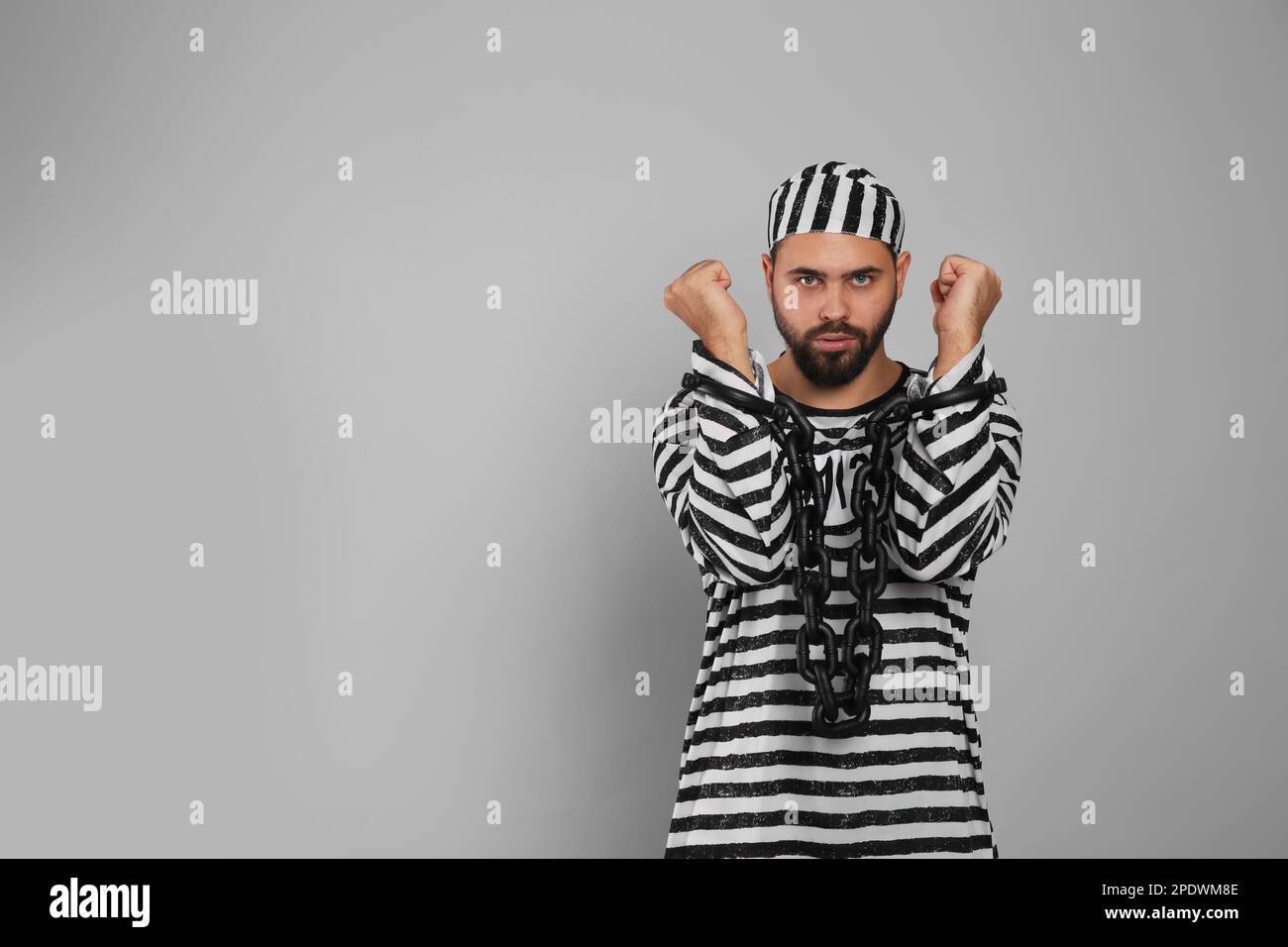 Prisoner in special uniform with chained hands on grey background ...