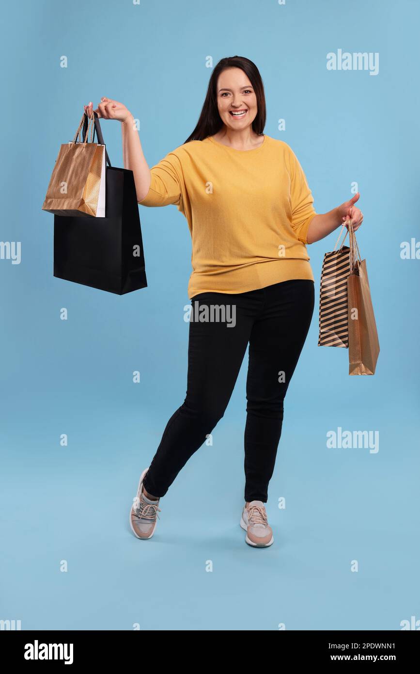 Beautiful overweight woman with shopping bags on turquoise background ...