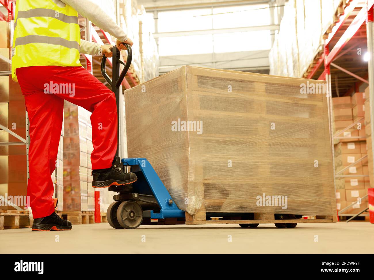 Worker moving wrapped wooden pallets with manual forklift in warehouse ...